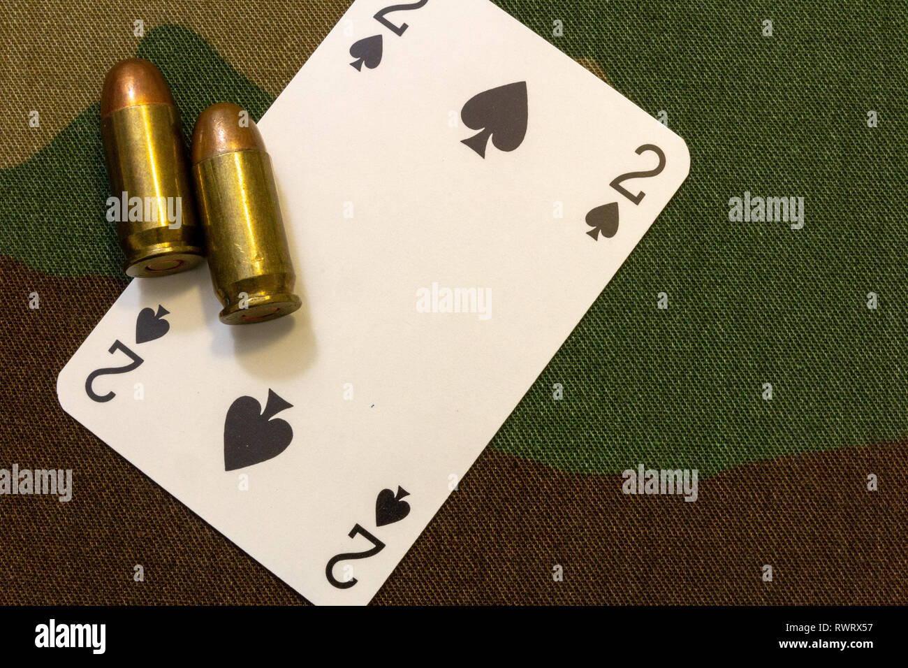 Two vintage pistol bullets and playing card on military camouflage ...