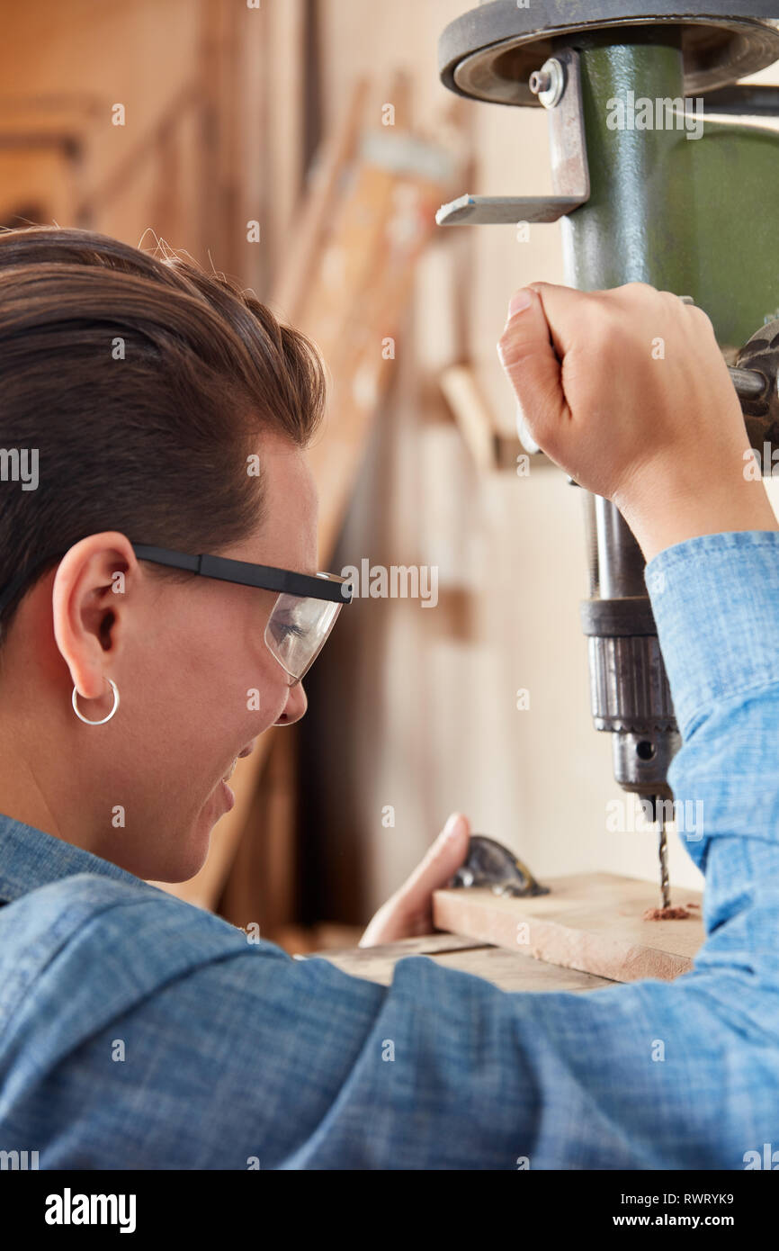 Young woman as a carpenter apprentice is learning at the drill in ...