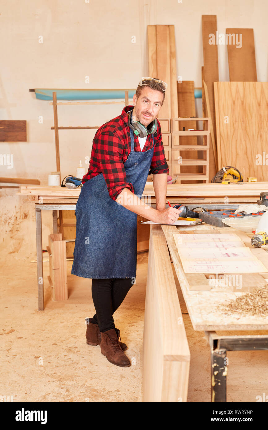 Joiner or carpenter in his workshop with clipboard at the workbench ...