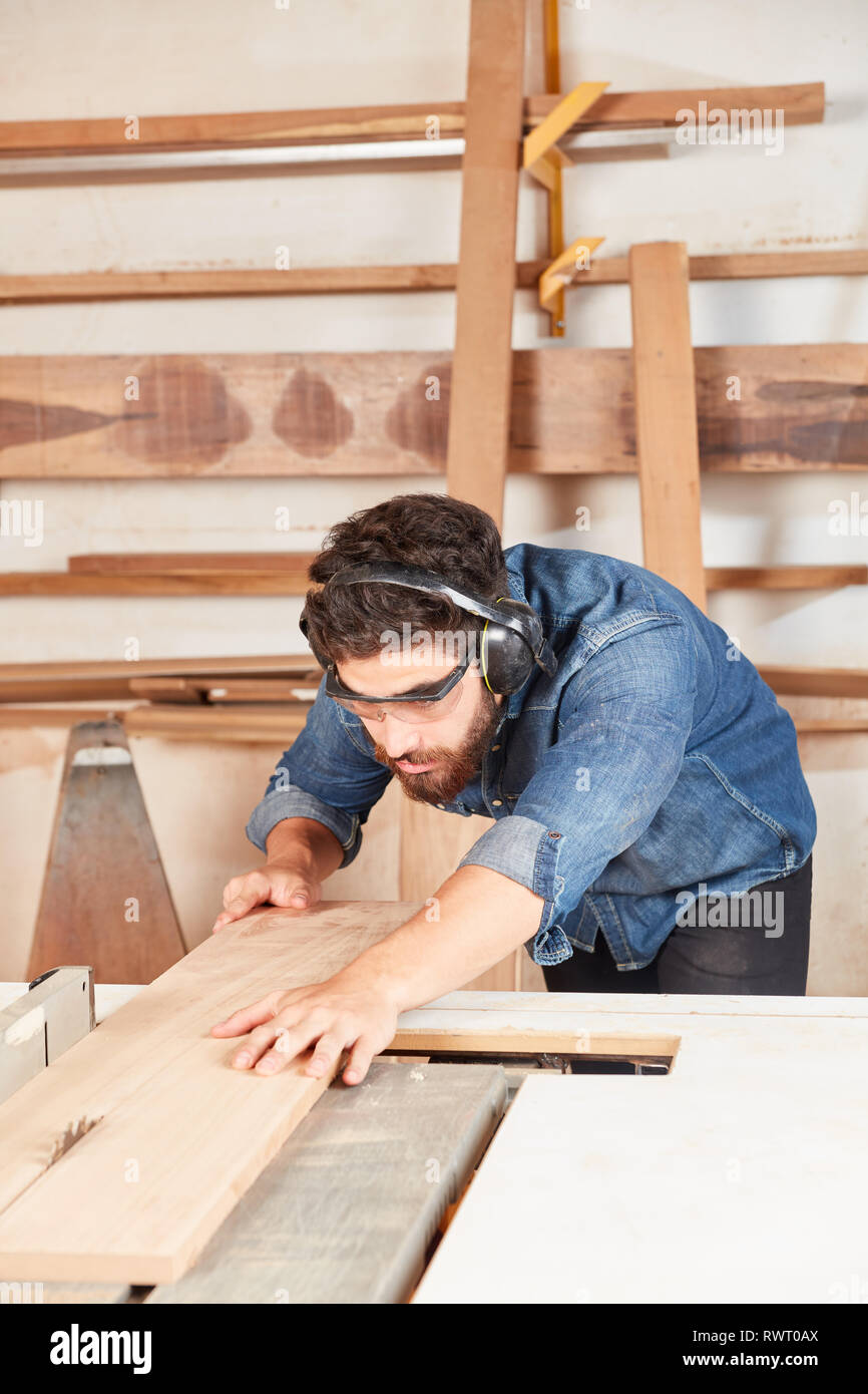 Young carpenter apprentice with ear protection saws wood at the ...