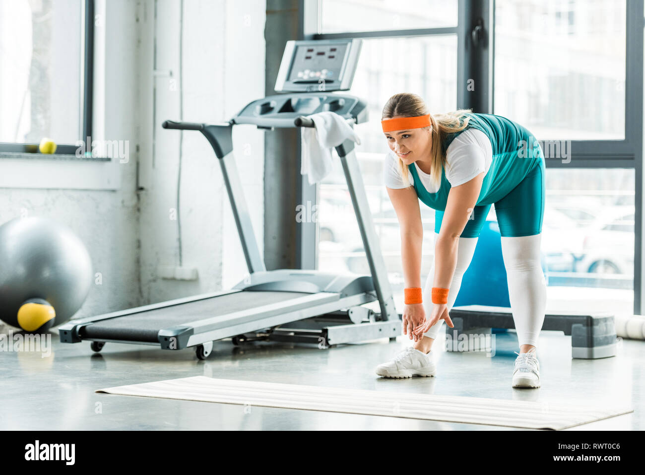 overweight woman stretching near fitness mat and treadmill in gym Stock ...