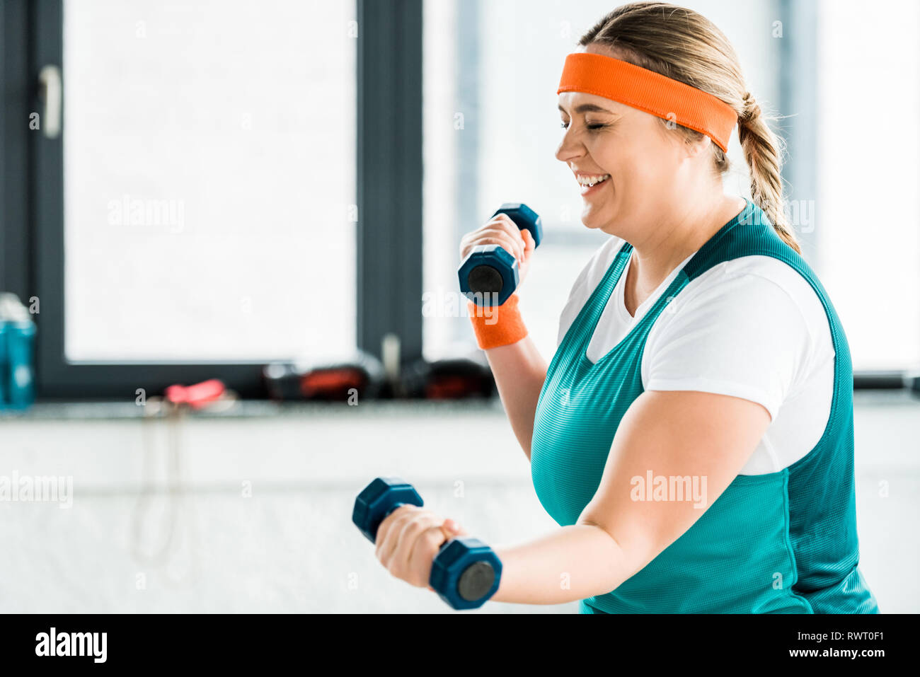 plus size woman exercising with dumbbells and laughing in gym Stock ...