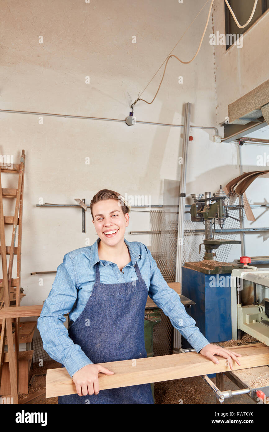 Laughing young woman as carpenter apprentice works with wood at the ...