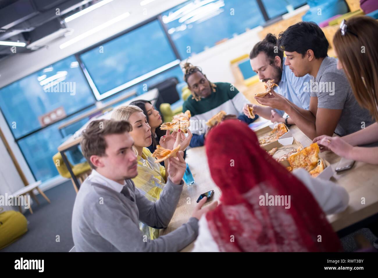 Friendly diverse multiethnic business team eating sharing pizza together in startup office ...