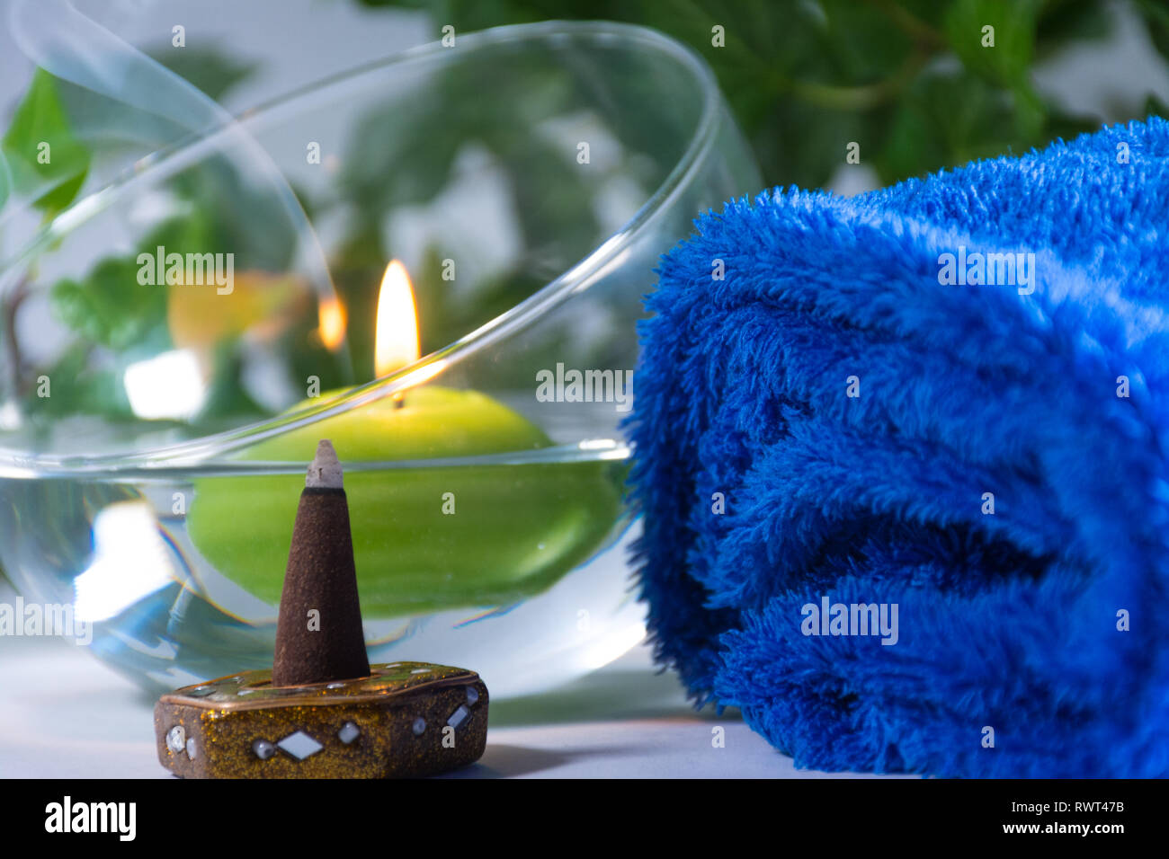 Lit candle with incense, some leaves and a blue towel, in a bathroom or ...
