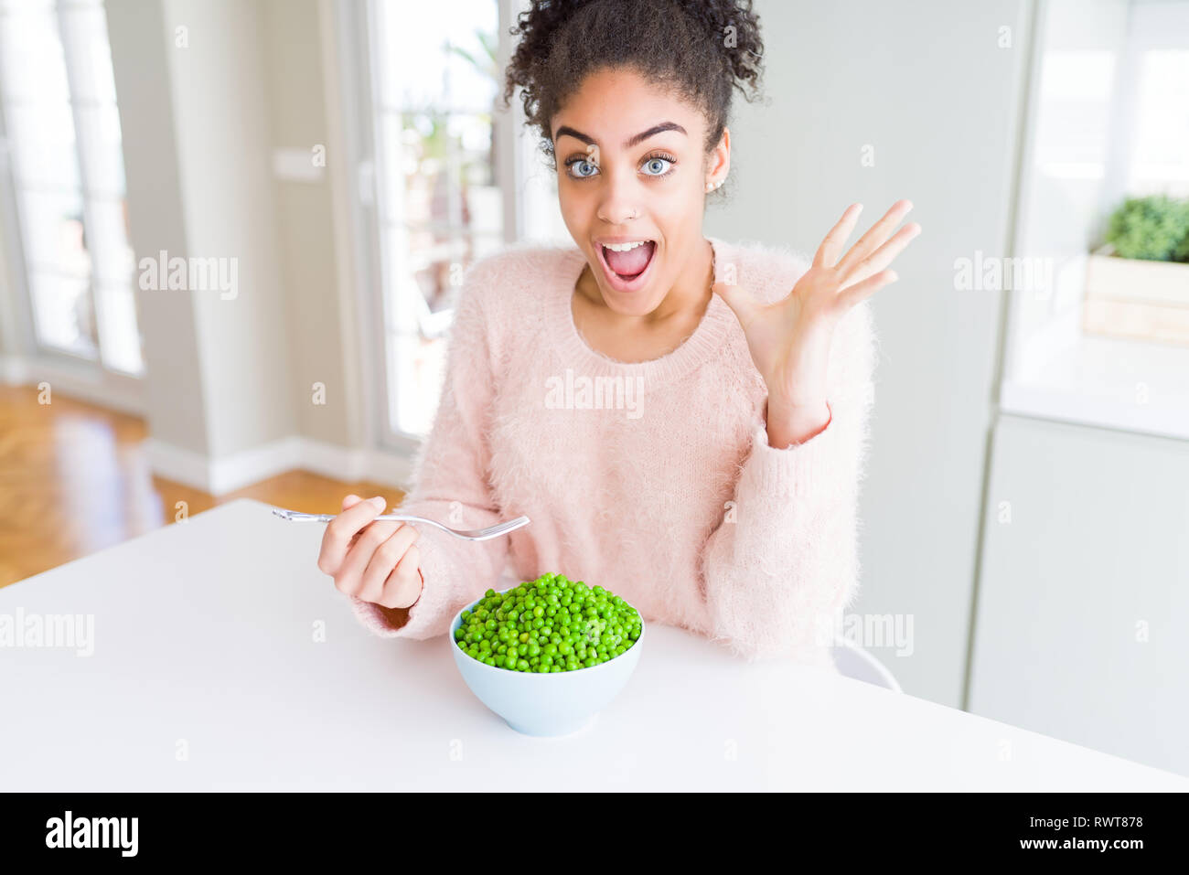 Young african american girl eating healthy green peas very happy and excited, winner expression ...