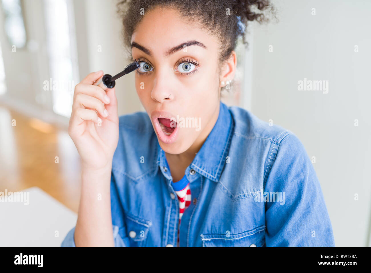 Young african american girl applying eyelashes mascara scared in shock ...