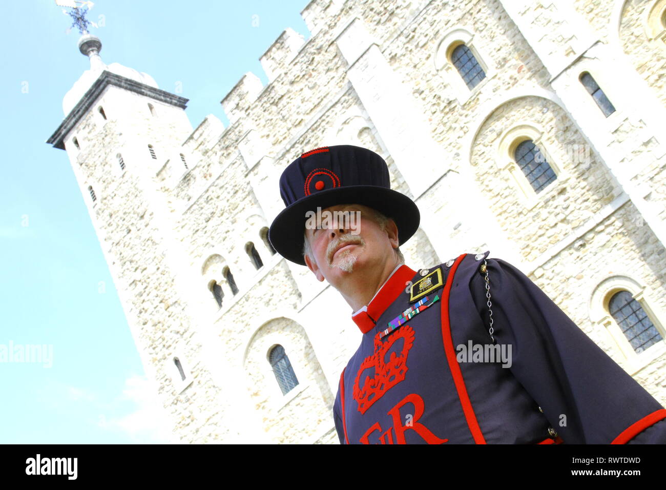 A Beefeater stands in front of The Tower of London on a bright sunny ...