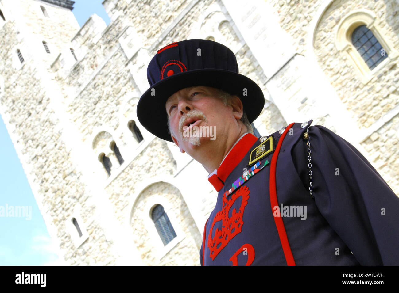 A Beefeater stands in front of The Tower of London on a bright sunny ...