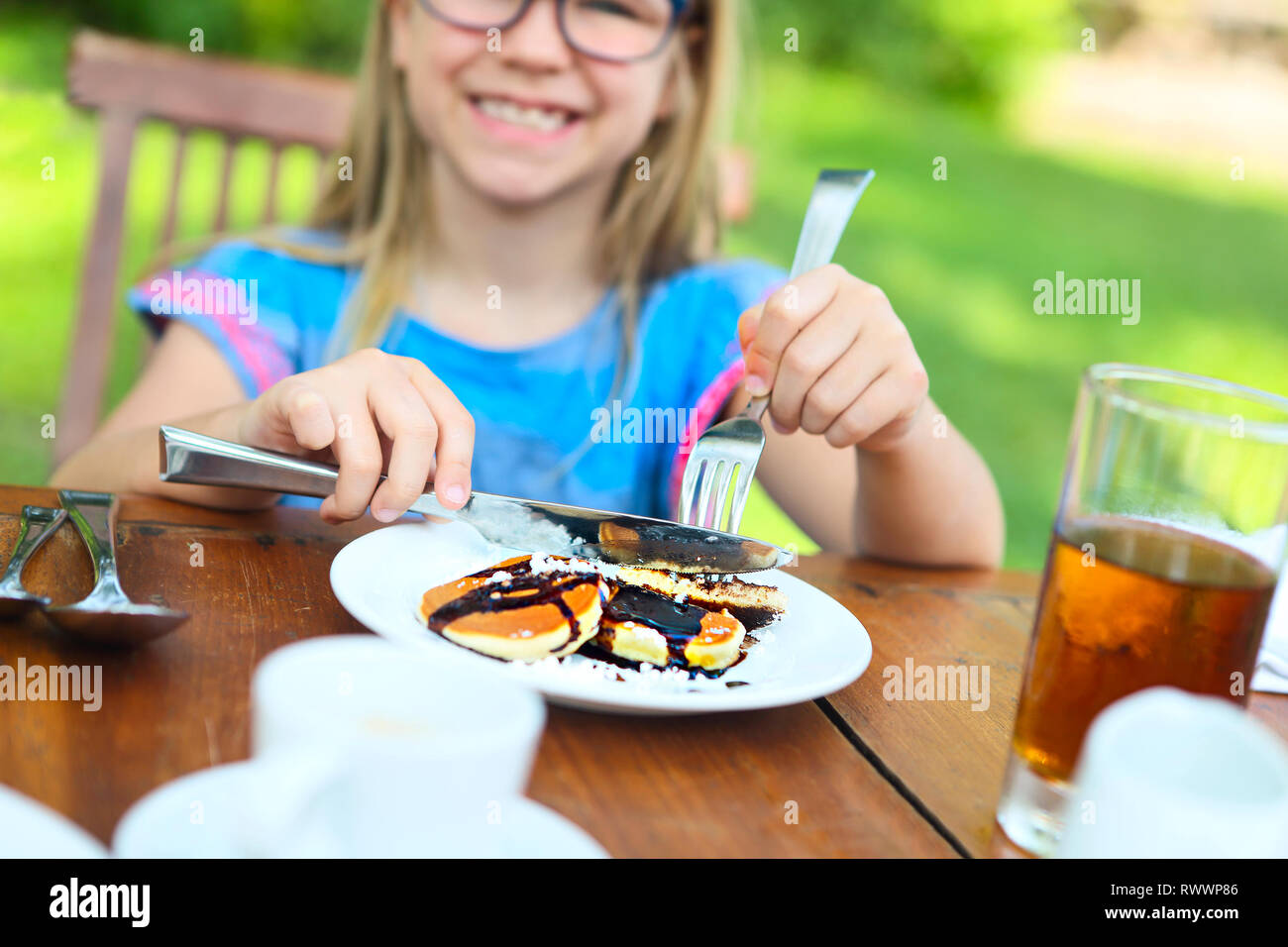 Little happy kid sitting at table and eating pancakes in the morning ...