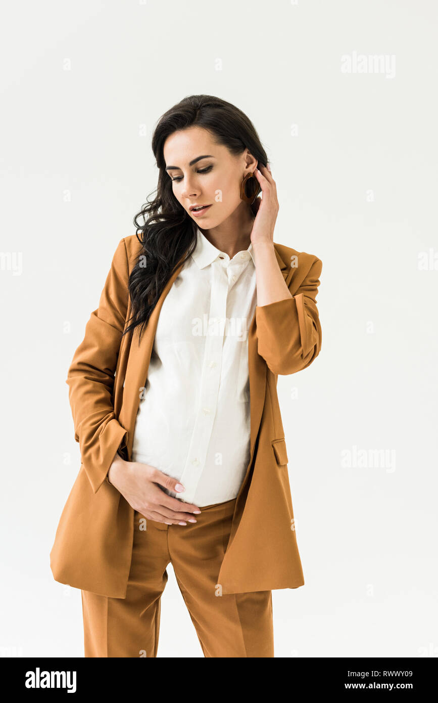 Pensive brunette pregnant woman in brown suit touching belly isolated ...