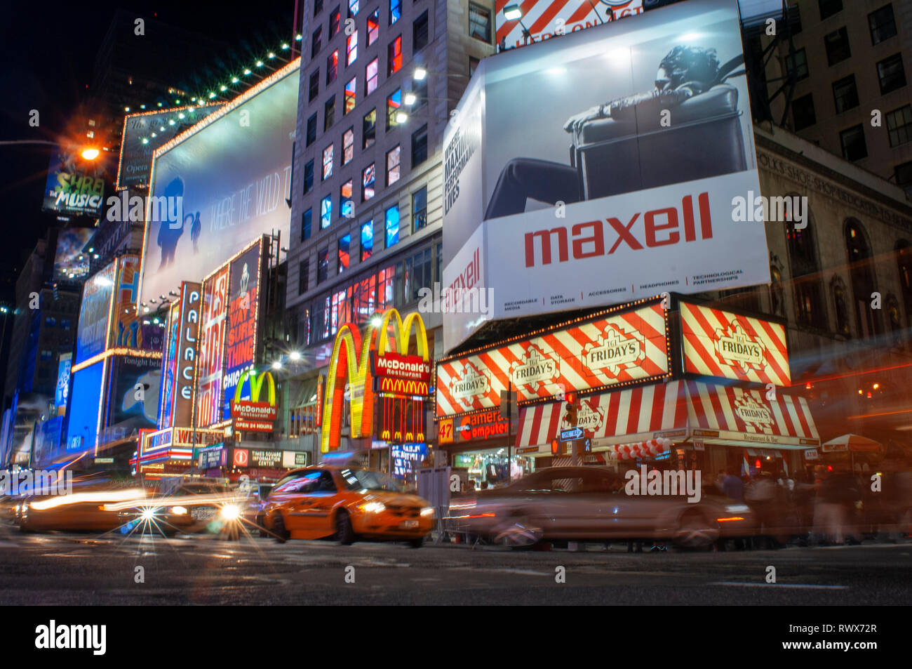 Bright neon signage flashes over crowds and taxi traffic zooming past ...