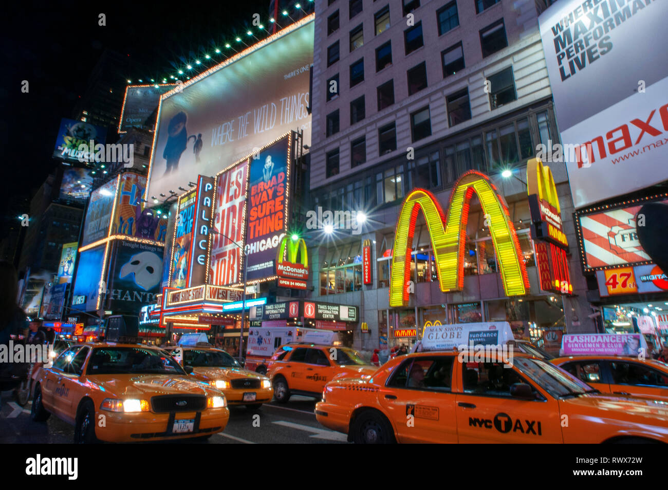 Bright neon signage flashes over crowds and taxi traffic zooming past ...