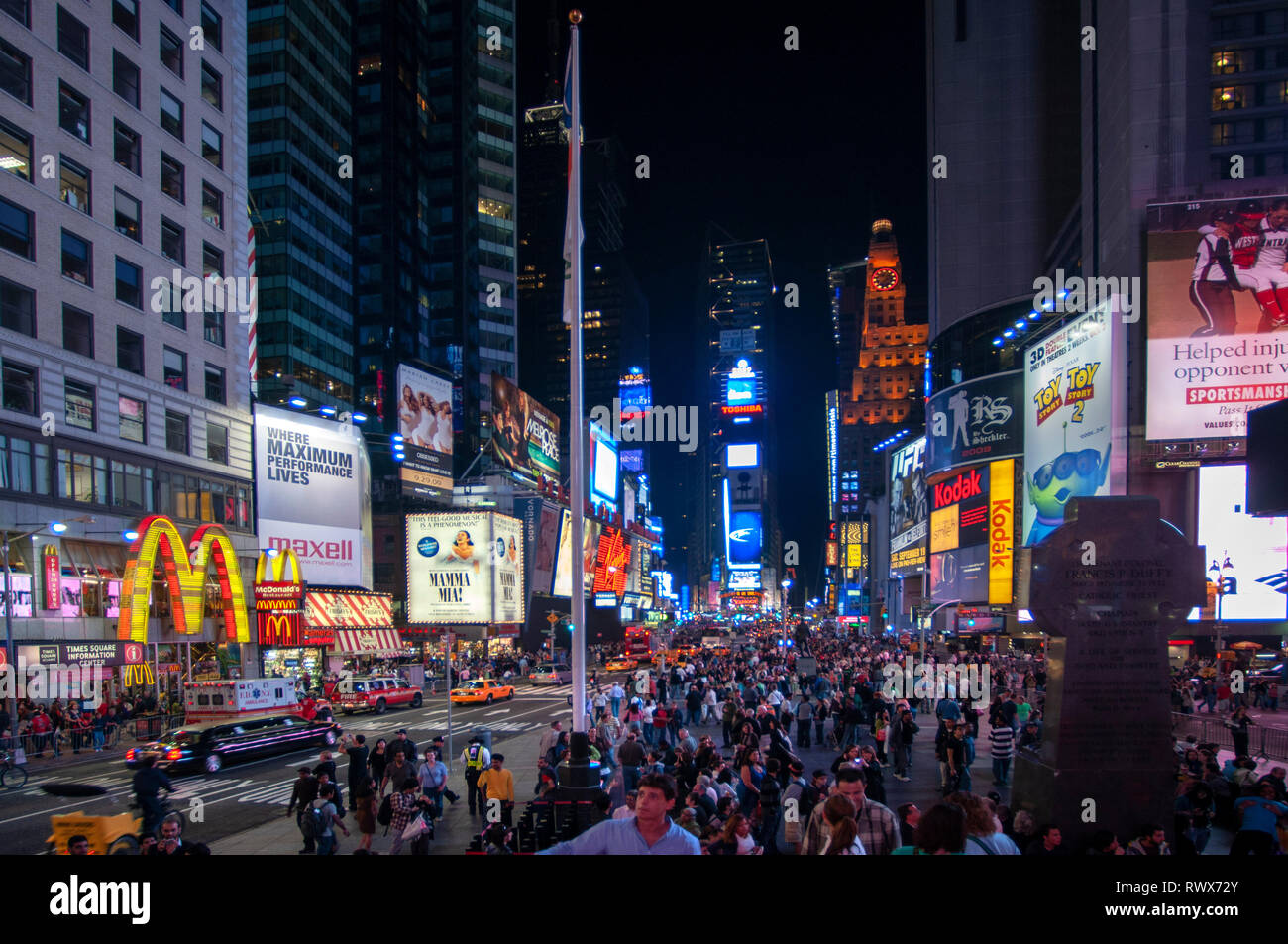 Bright neon signage flashes over crowds and taxi traffic zooming past ...