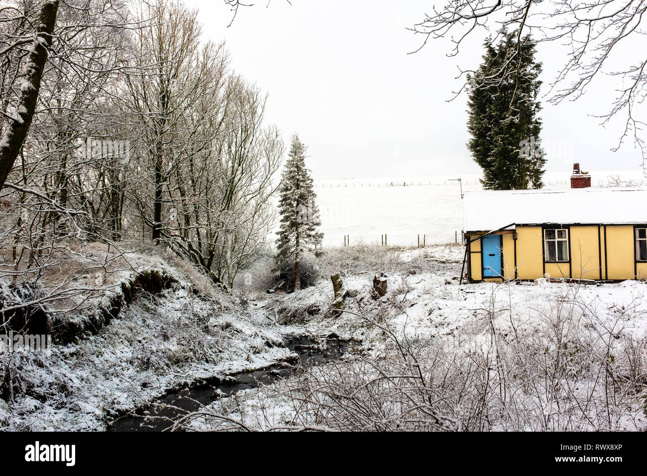 Cute prefabricated tumble down rural cottage in the snow by a stream ...