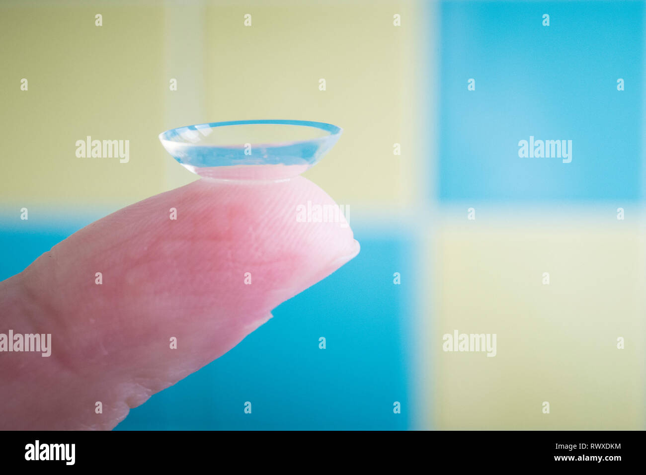 Soft contact lens on finger tip, macro with blue and yellow background ...