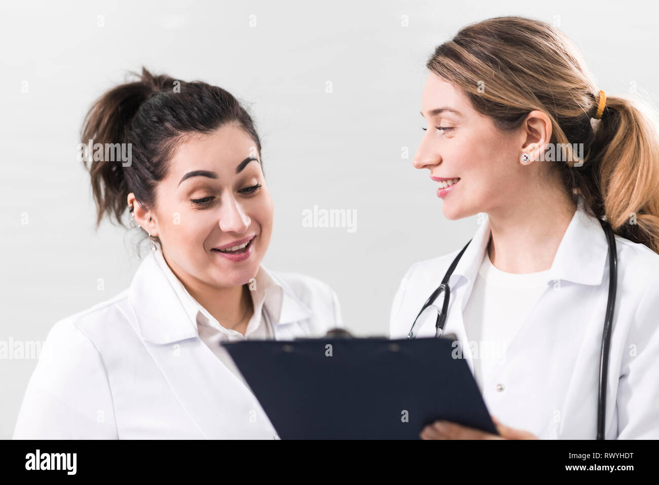 Two female assistants dressed in white coats talking to each other in ...