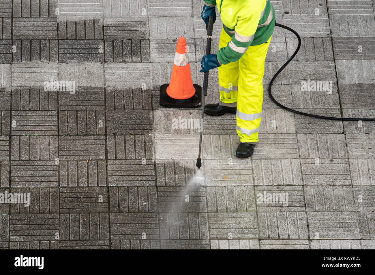 Worker cleaning the street sidewalk with high pressure water jet ...