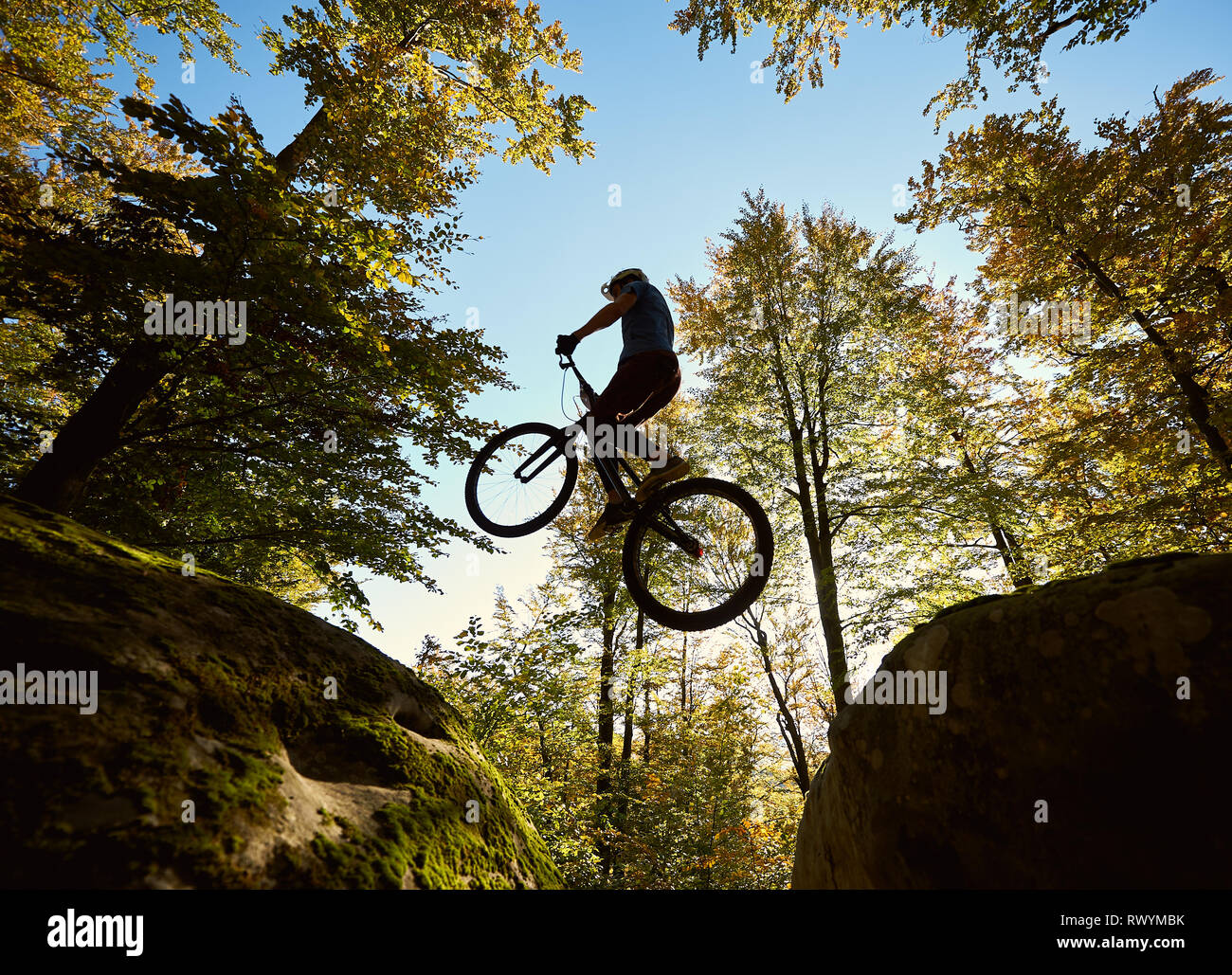 Young male biker jumping on trial bicycle between two big boulders ...