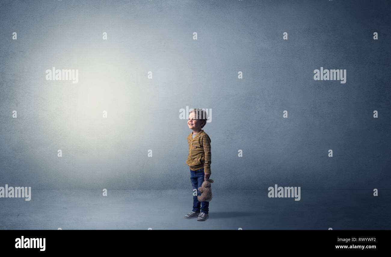 Little waggish kid staying alone in a big empty room with his plush ...