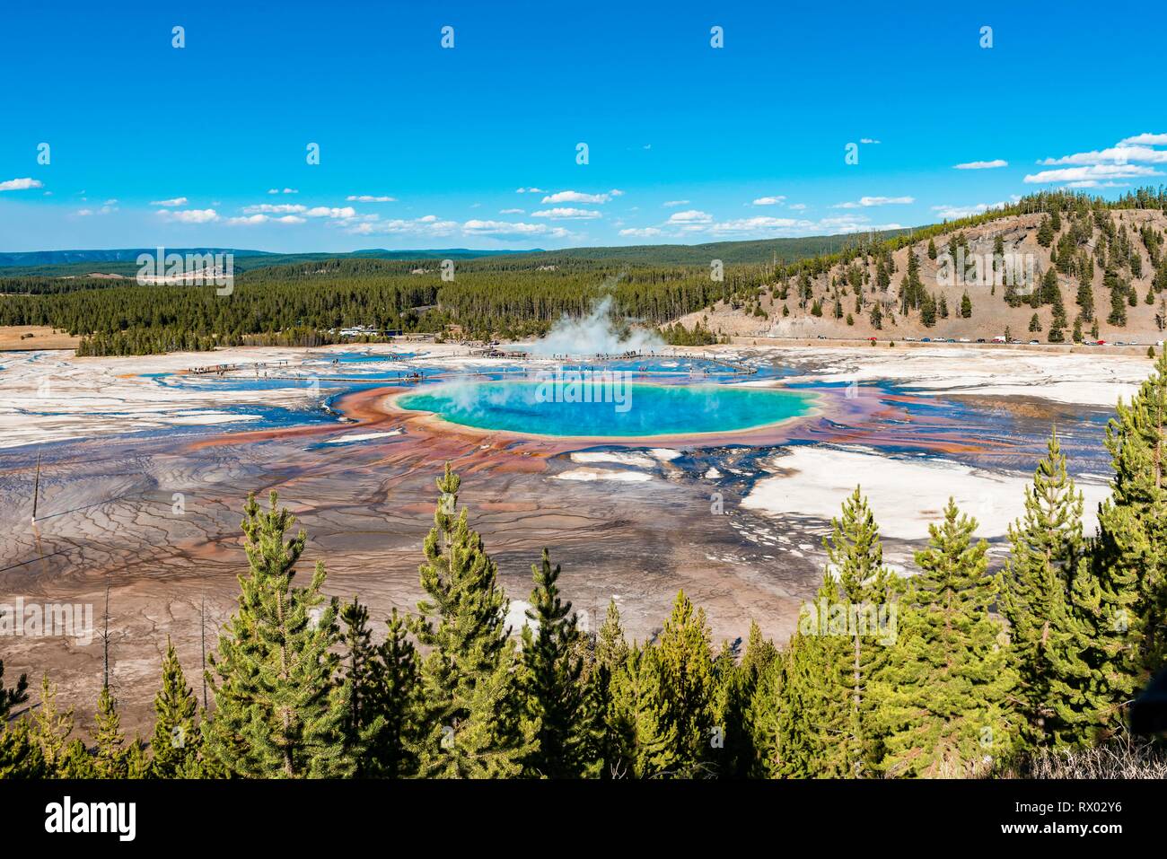 Visitors on footbridge over steaming hot spring with coloured mineral ...