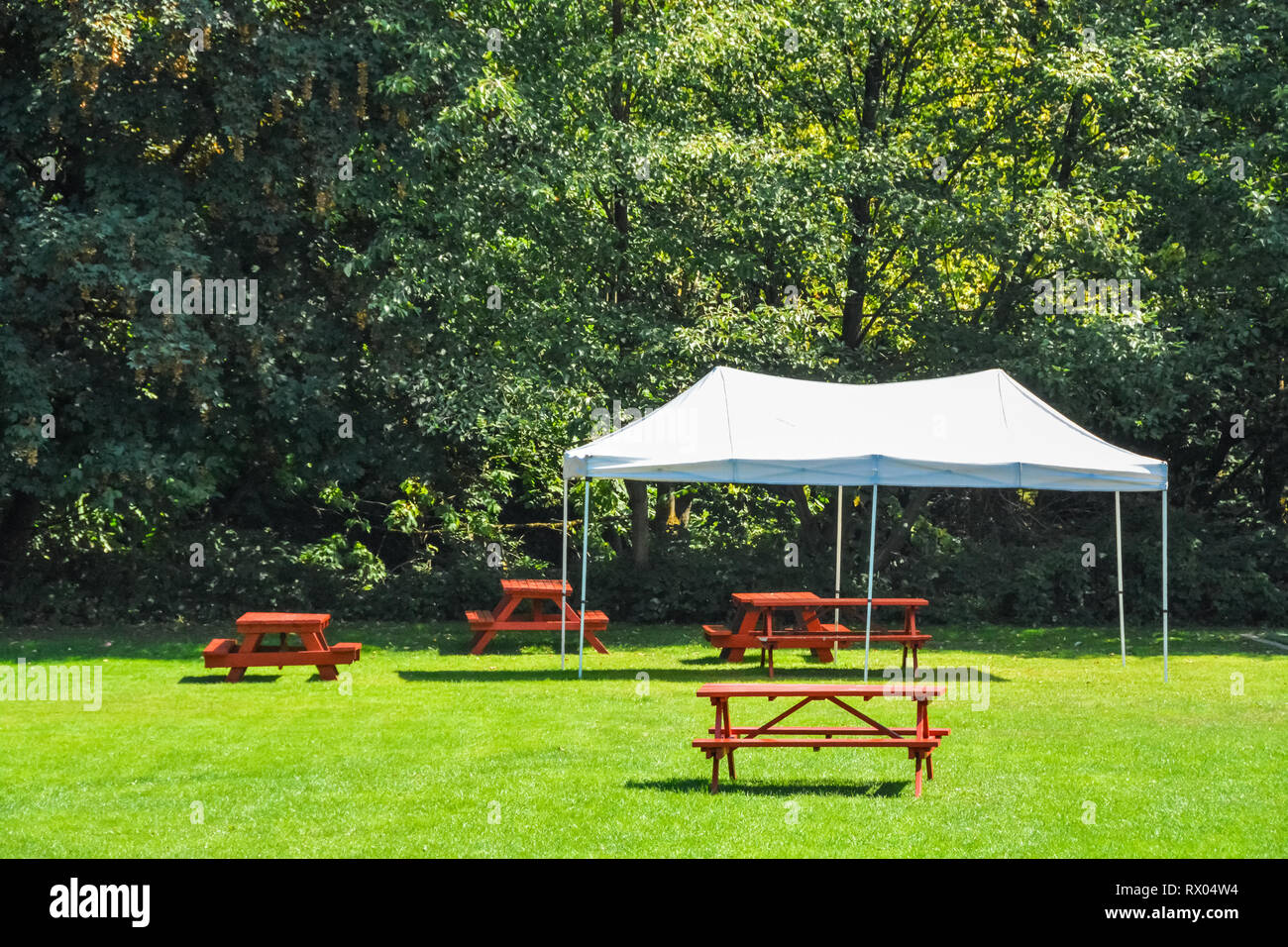 Rest area with red picnic tables and white tent on green lawn in a park ...