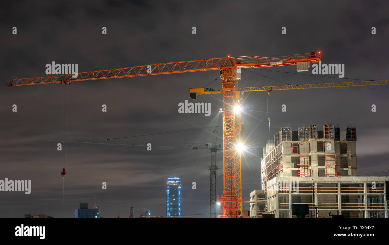 Tower cranes at a construction site in the night city. Electric light ...