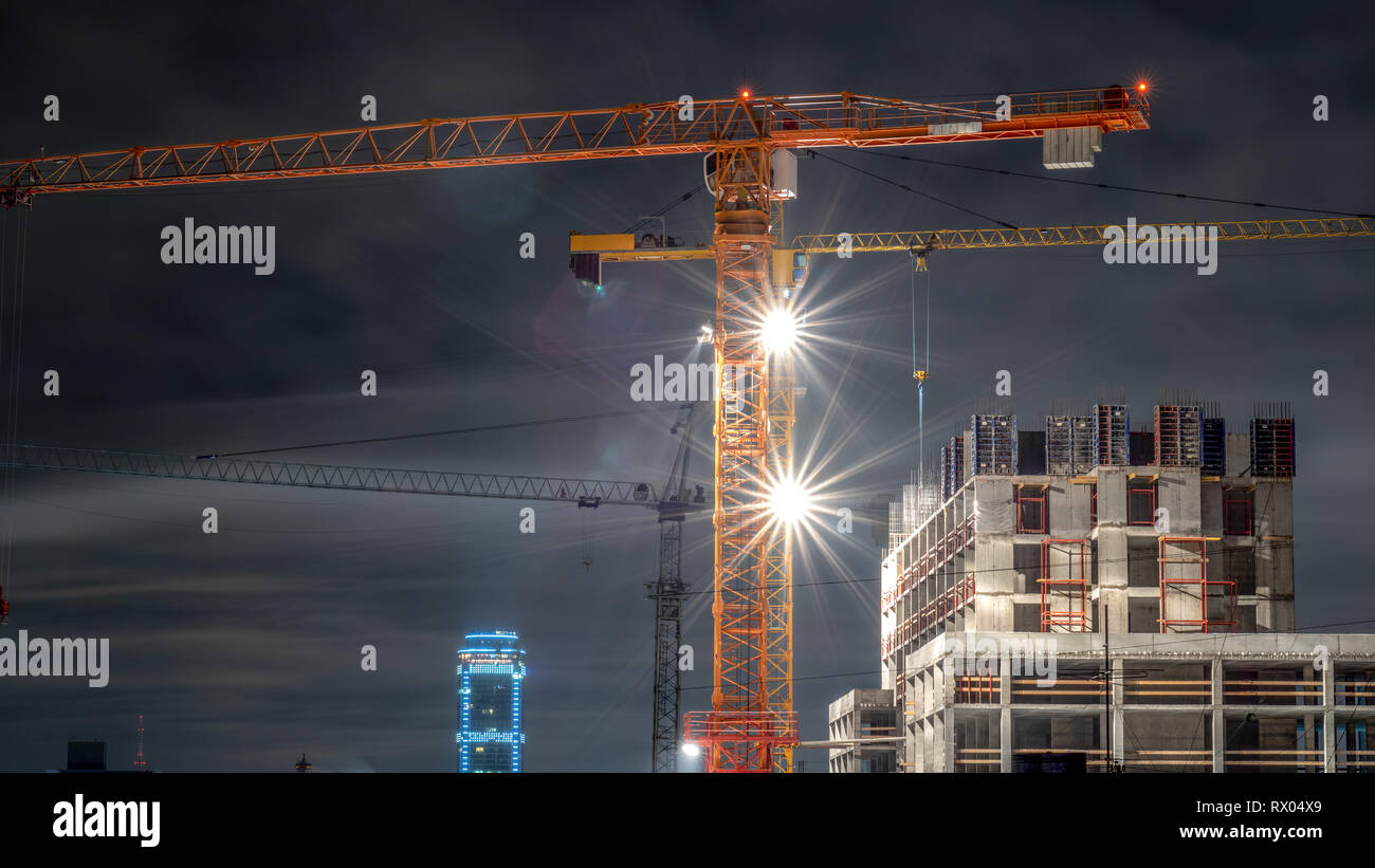 Tower cranes at a construction site in the night city. Electric light ...