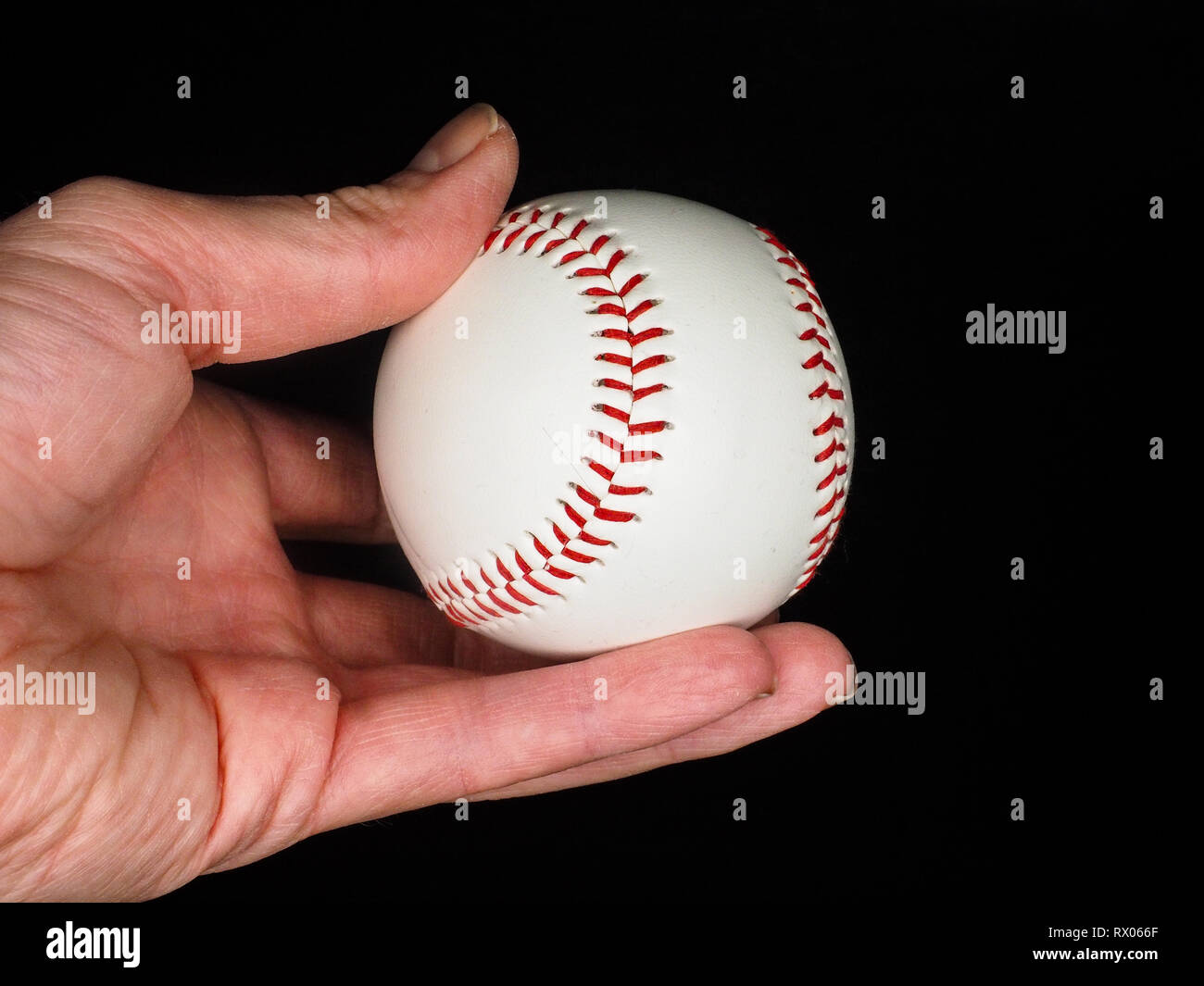 Baseball, white and red with threads in hand against black background ...