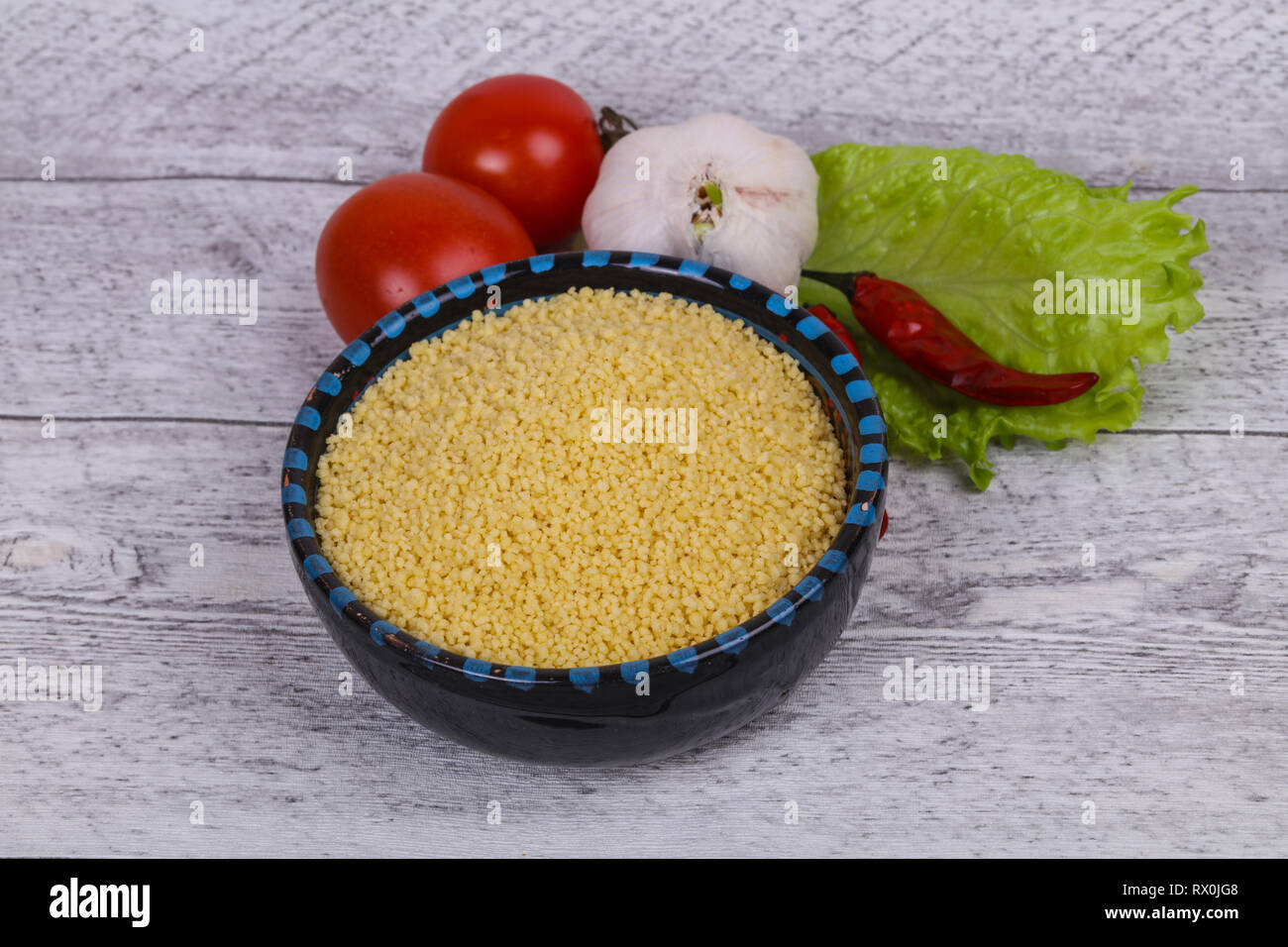 Raw couscous in the bowl served salad leaves, tomato and pepper ready ...