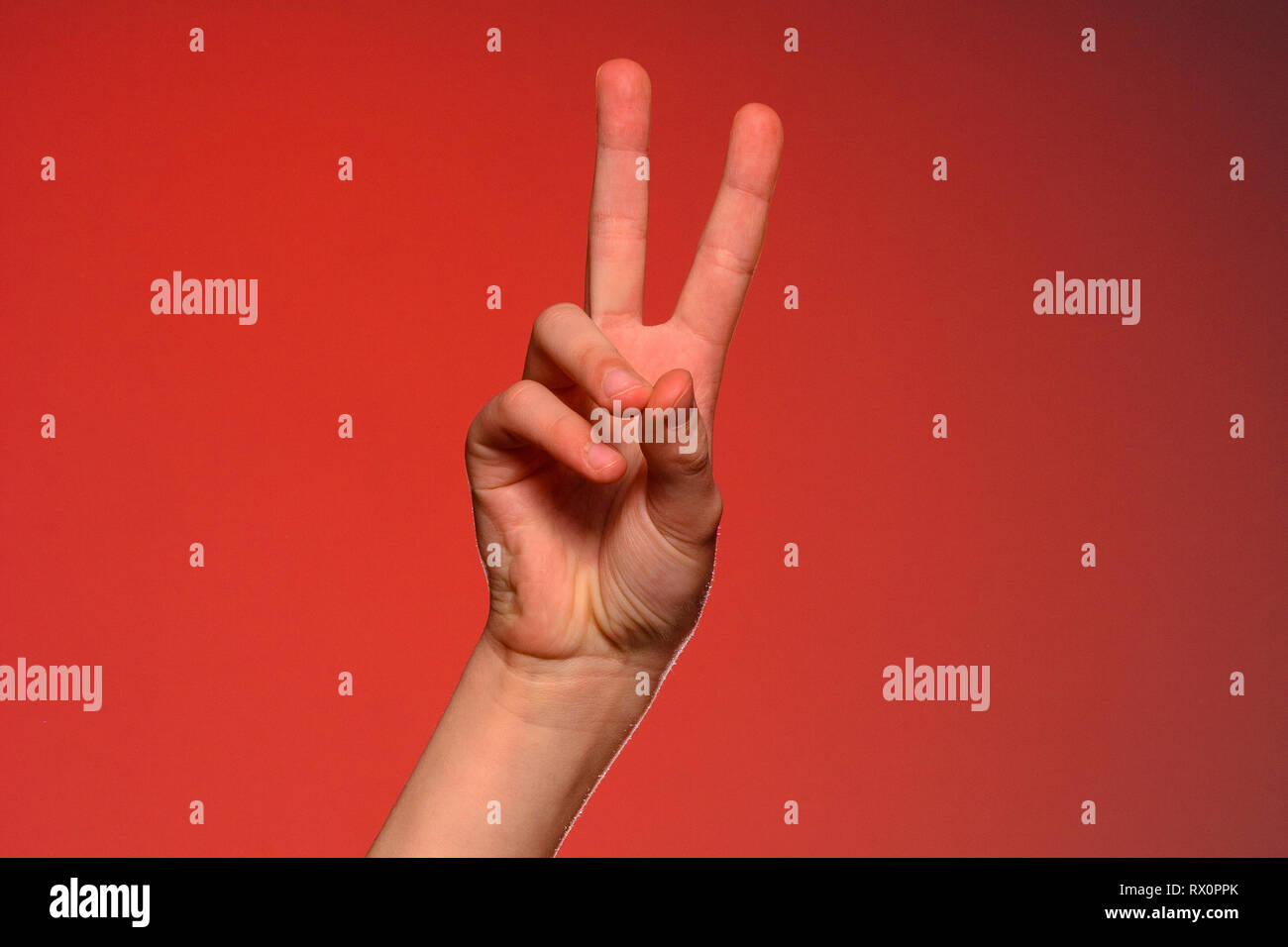 The soft hand showing the victory sign is isolated on a red background ...