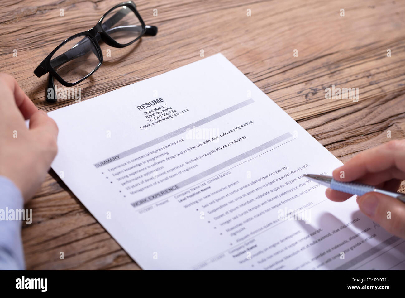 Close-up Of Businessman Holding Pen In Hand Reading Resume On Wooden ...