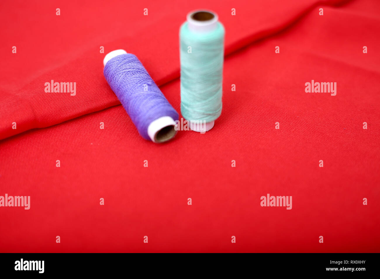 Spool of two sewing thread on the red cloth Stock Photo - Alamy