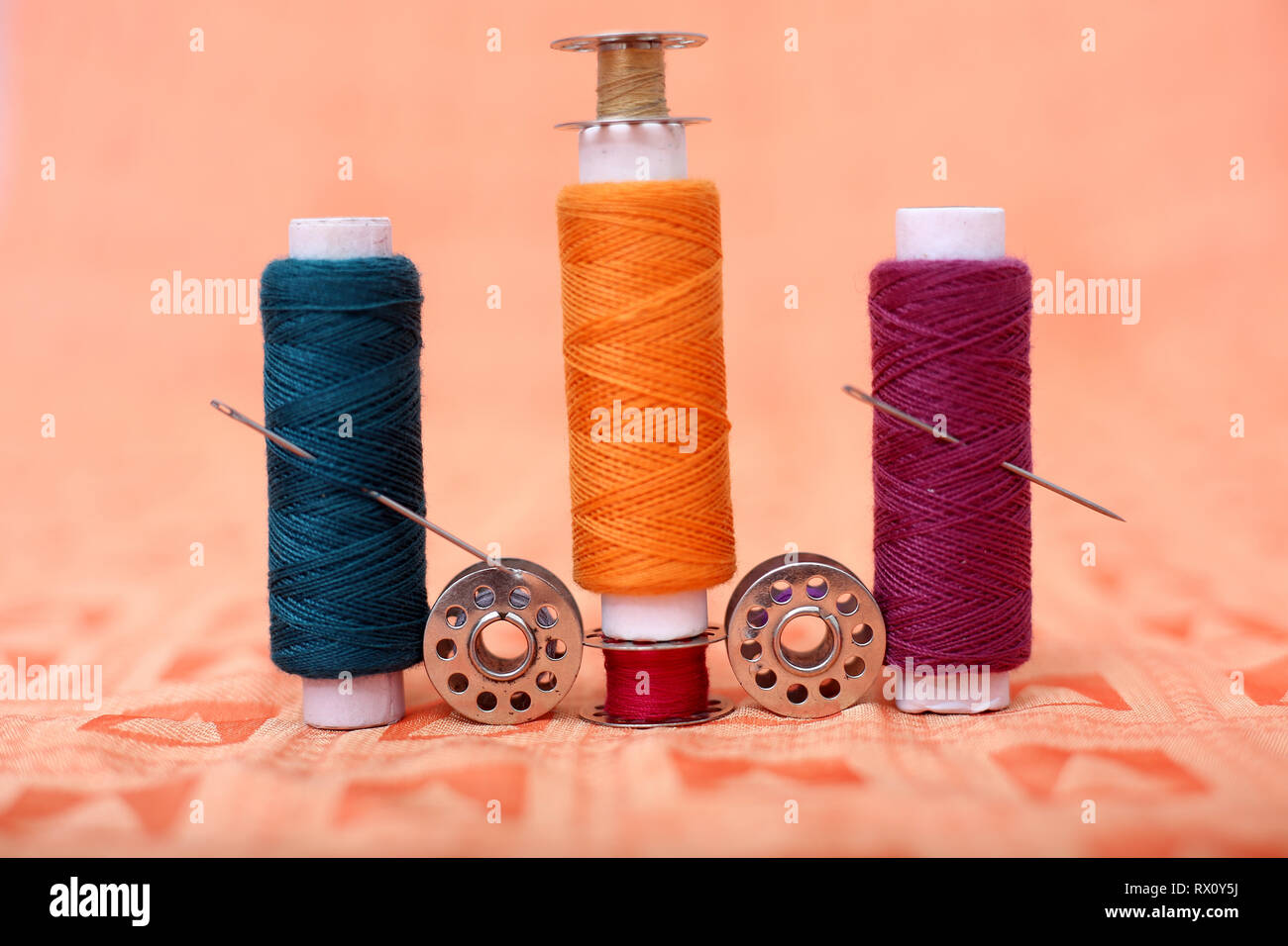 Picture of sewing thread and bobbin with needle on the orange cloth ...
