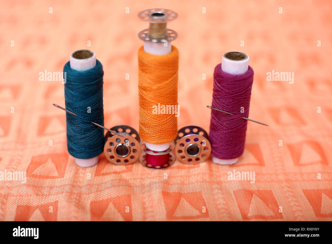 Picture of sewing thread and bobbin with needle on the orange cloth ...