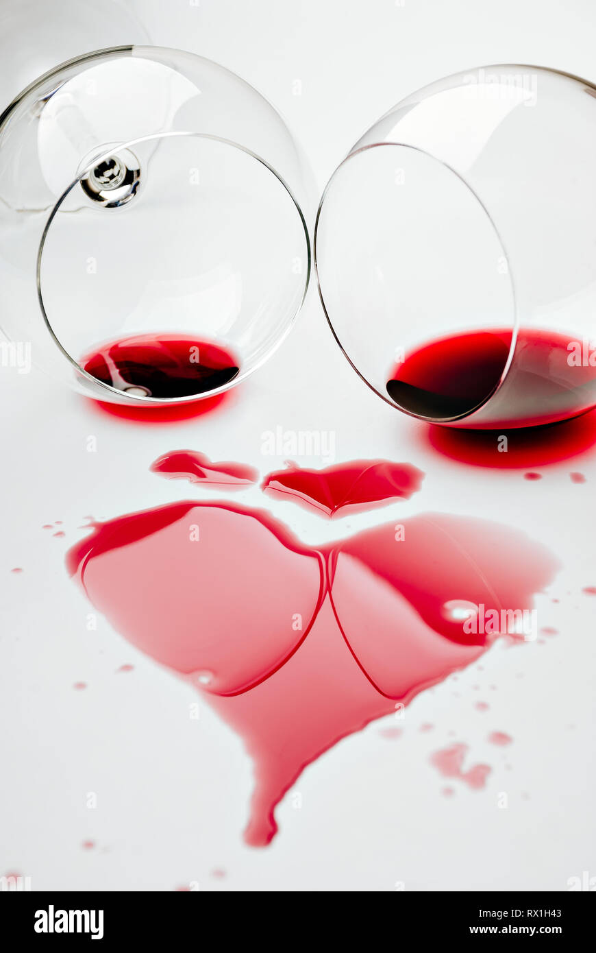 Red wine spilled from two turned wineglasses making a heart shape over ...