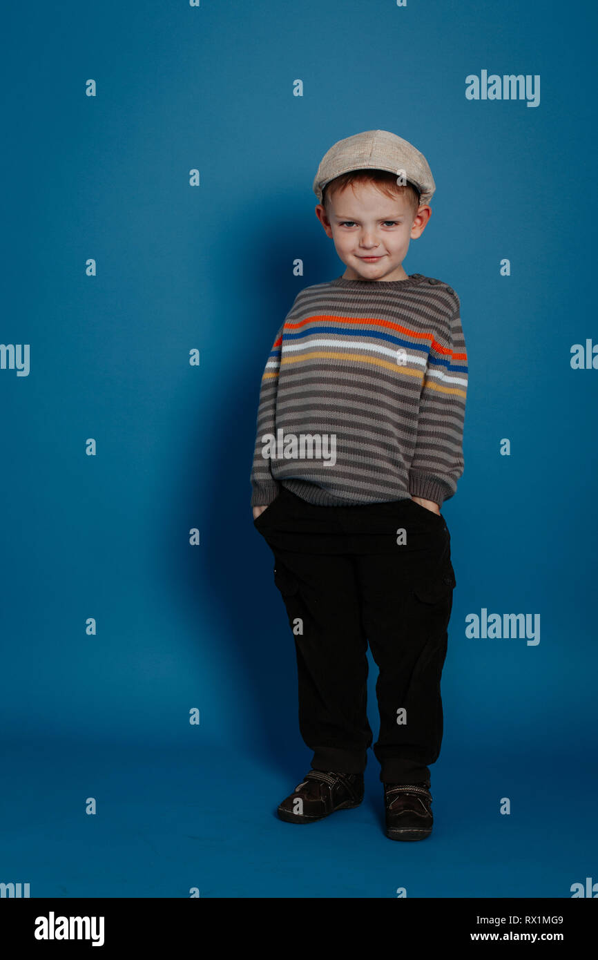 A little boy in a cap is posing and smiling. Hands in pockets. On a ...