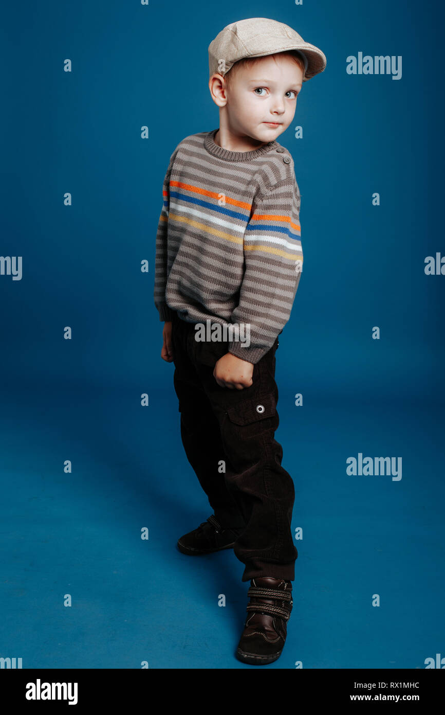 A little boy in a cap is posing and smiling. Hands in pockets. On a ...