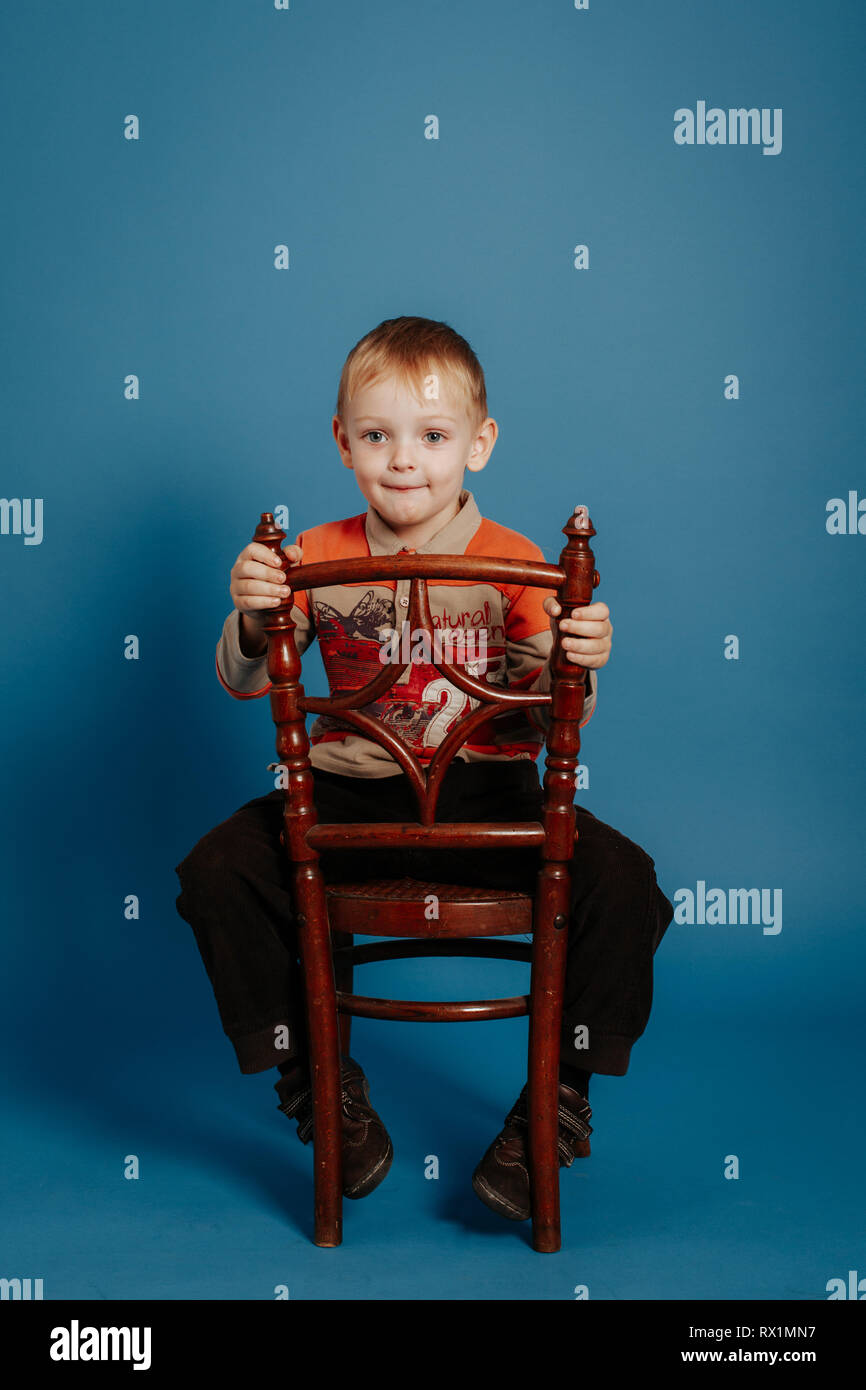 A little boy in a cap sits on a chair and smiles. On a blue background ...