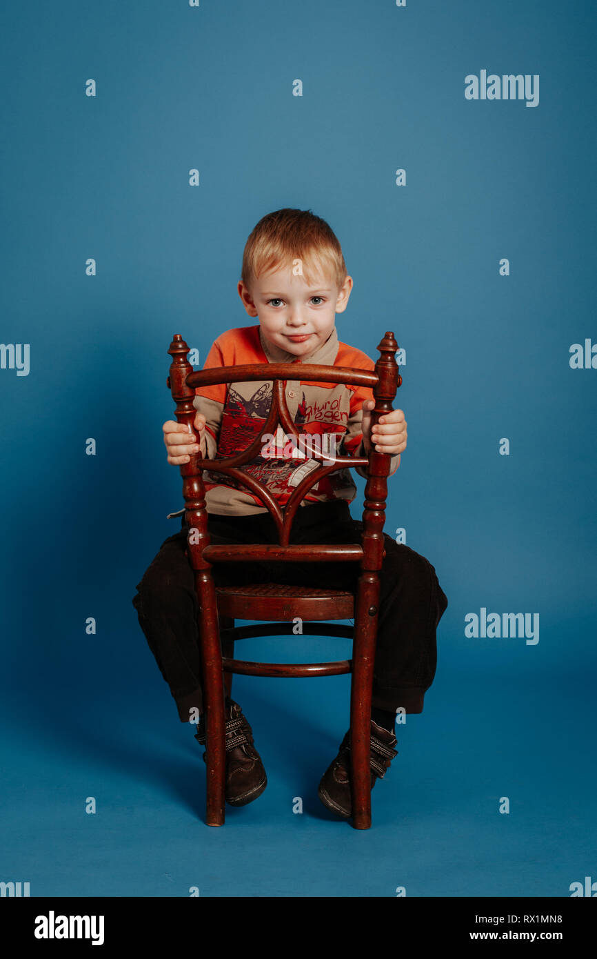 A little boy in a cap sits on a chair and smiles. On a blue background ...