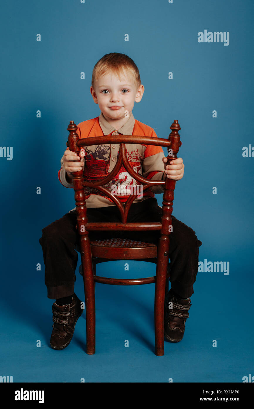 A little boy in a cap sits on a chair and smiles. On a blue background ...