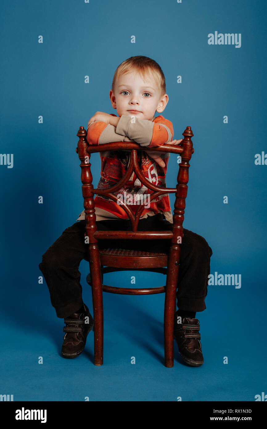 A little boy in a cap sits on a chair and thinks. On a blue background ...