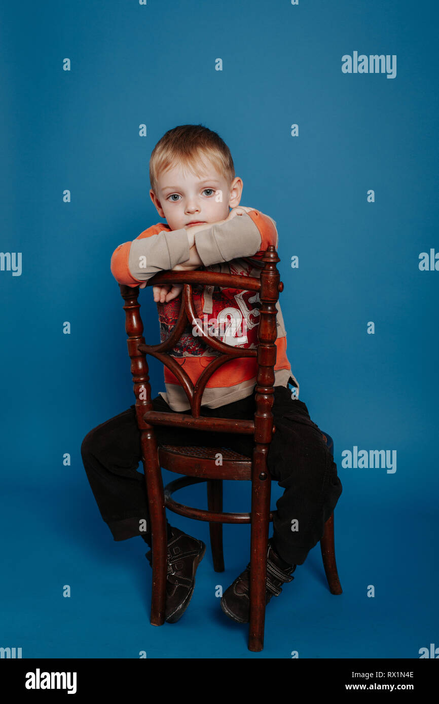 A little boy in a cap sits on a chair and thinks. On a blue background ...