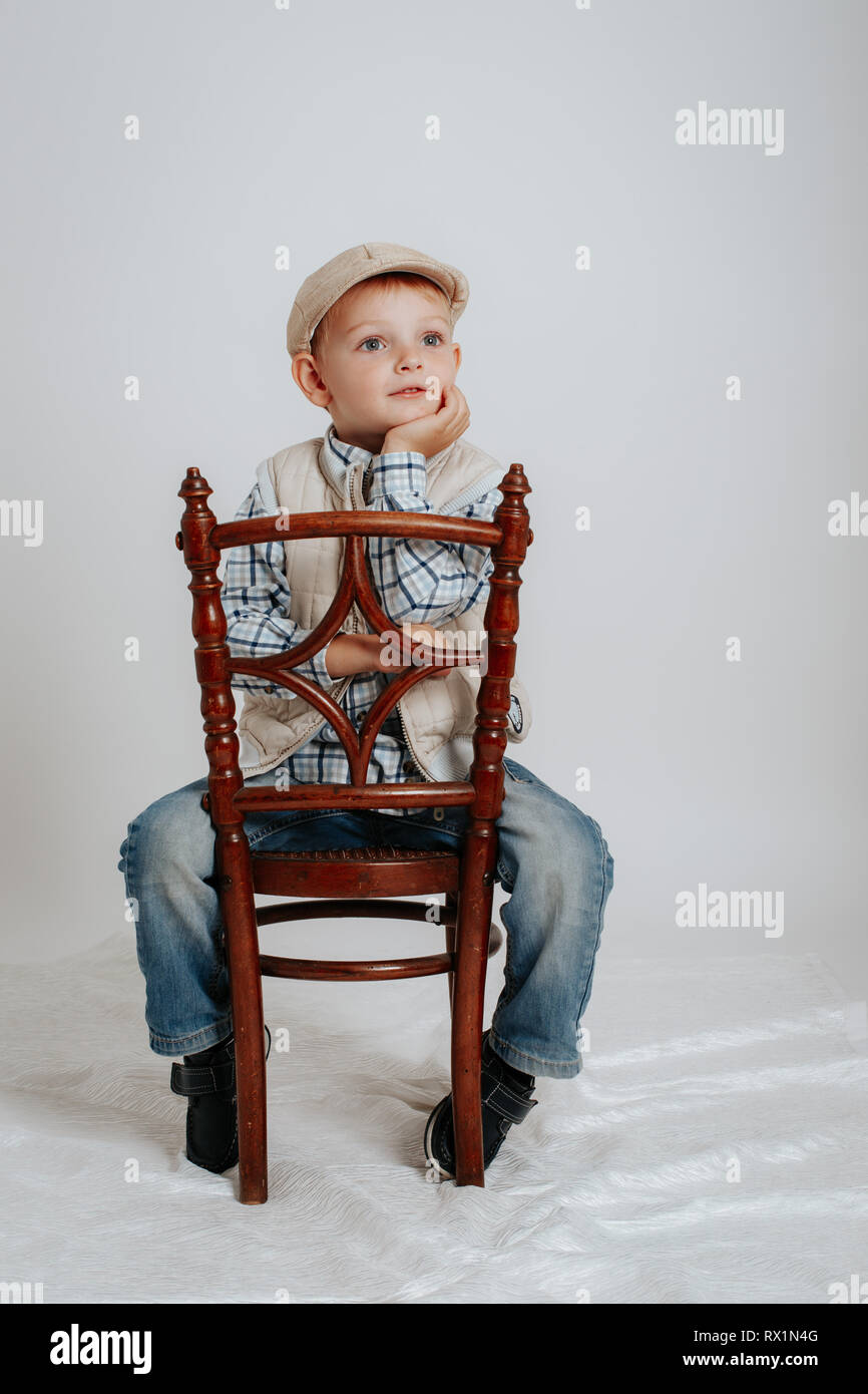 A little boy in a cap sits on a chair and thinks. On a white background ...