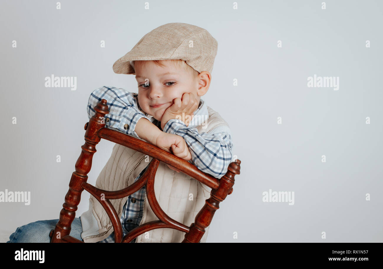 A little boy in a cap sits on a chair and thinks. On a white background ...