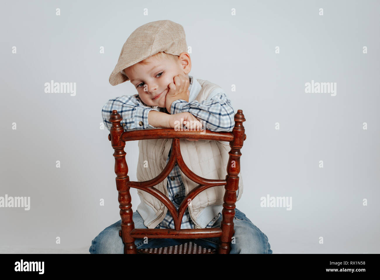 A little boy in a cap sits on a chair and thinks. On a white background ...