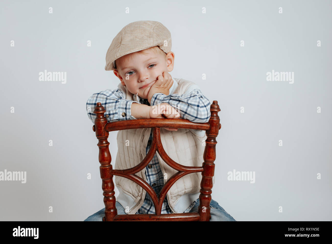 A little boy in a cap sits on a chair and thinks. On a white background ...
