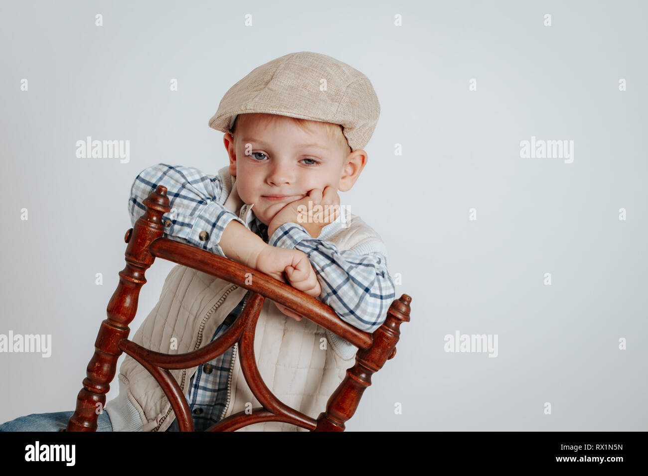 A little boy in a cap sits on a chair and thinks. On a white background ...