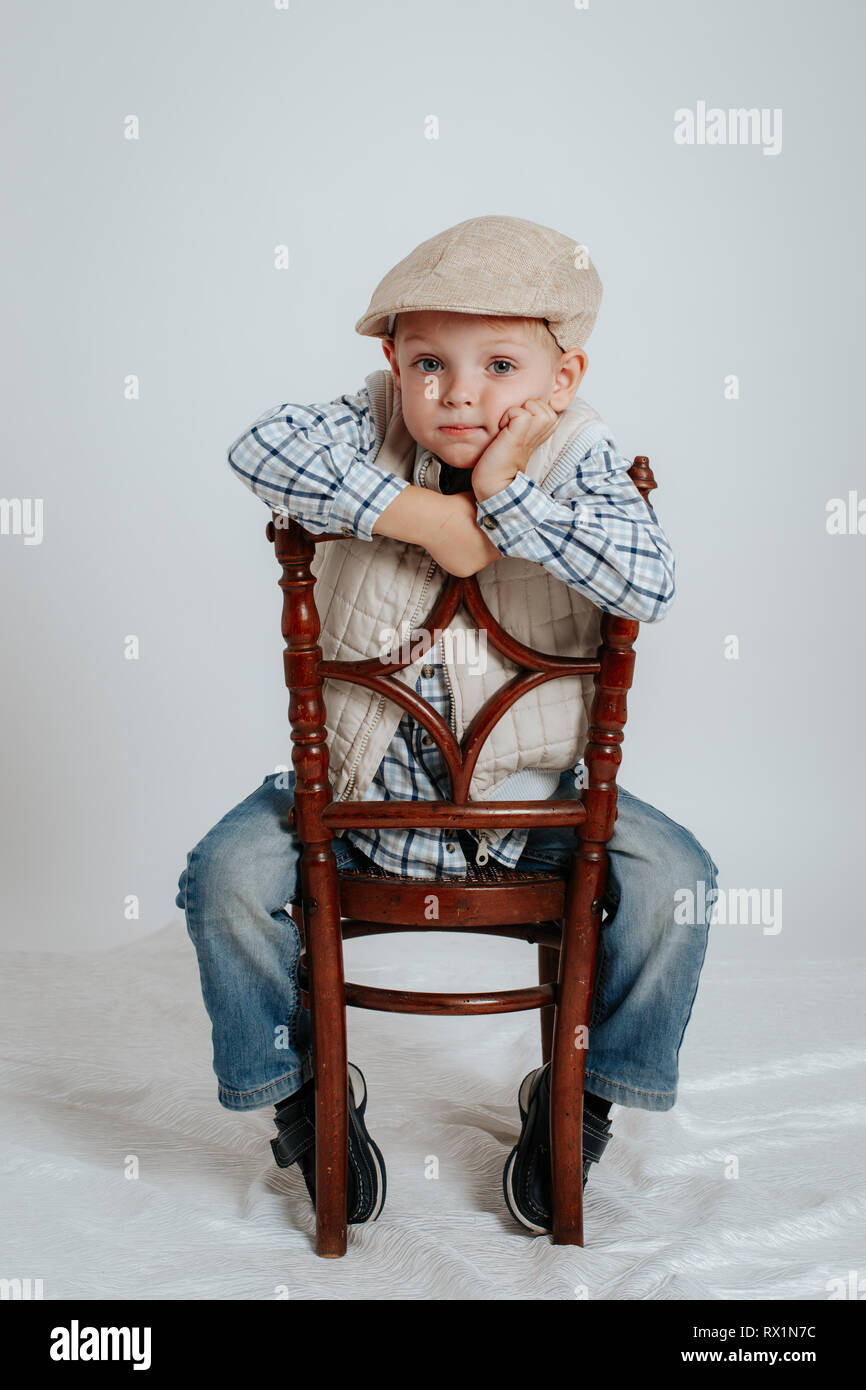 A little boy in a cap sits on a chair and thinks. On a white background ...