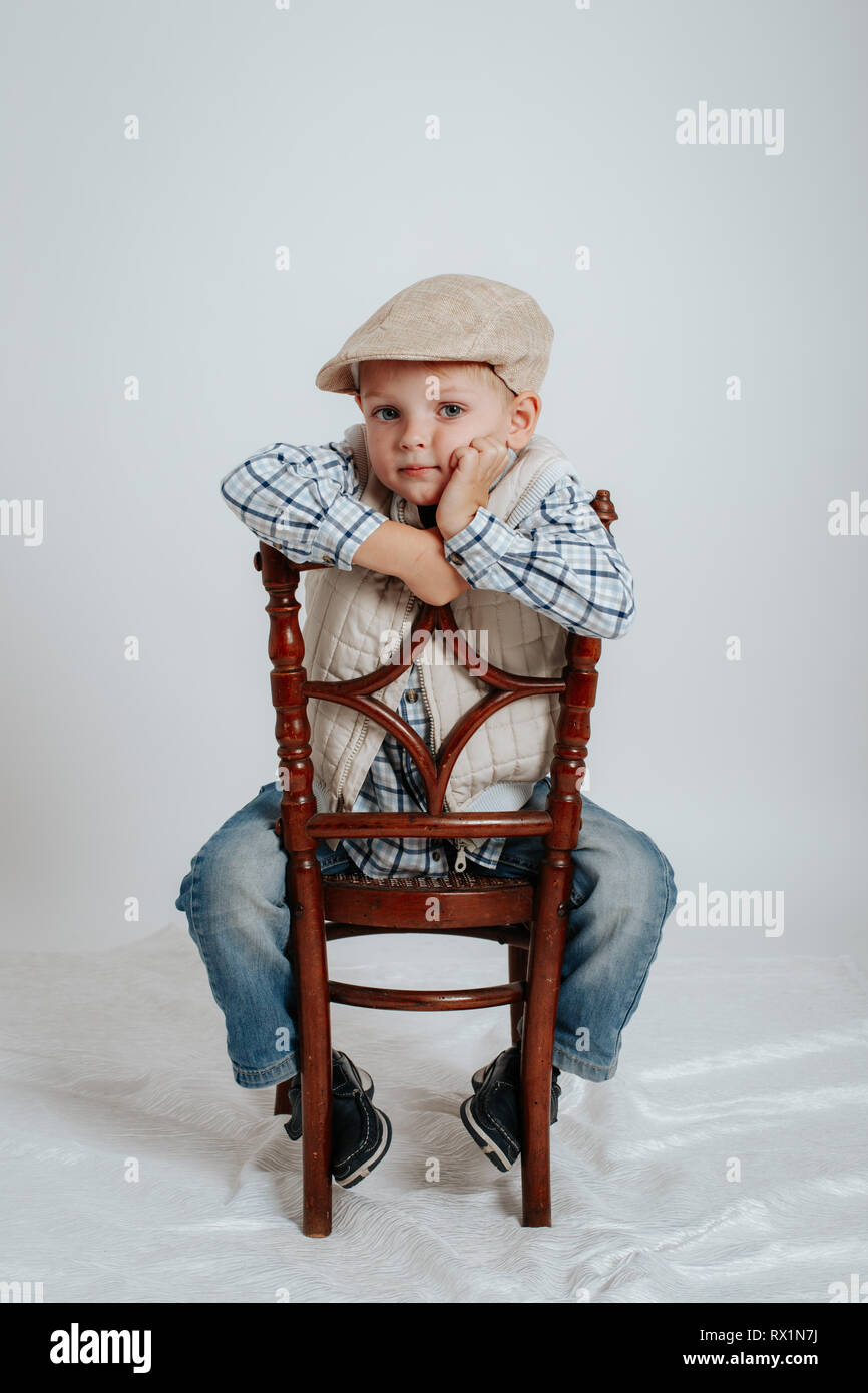 A little boy in a cap sits on a chair and thinks. On a white background ...